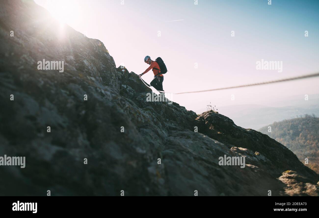 Mountaineer with backpack using climbing rope to climb rocky mountain ...