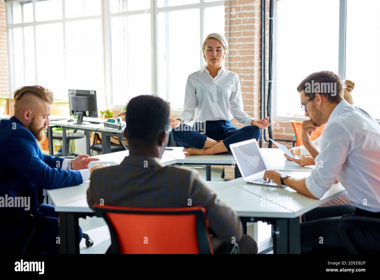 young caucasian woman meditating in office while colleagues are working ...