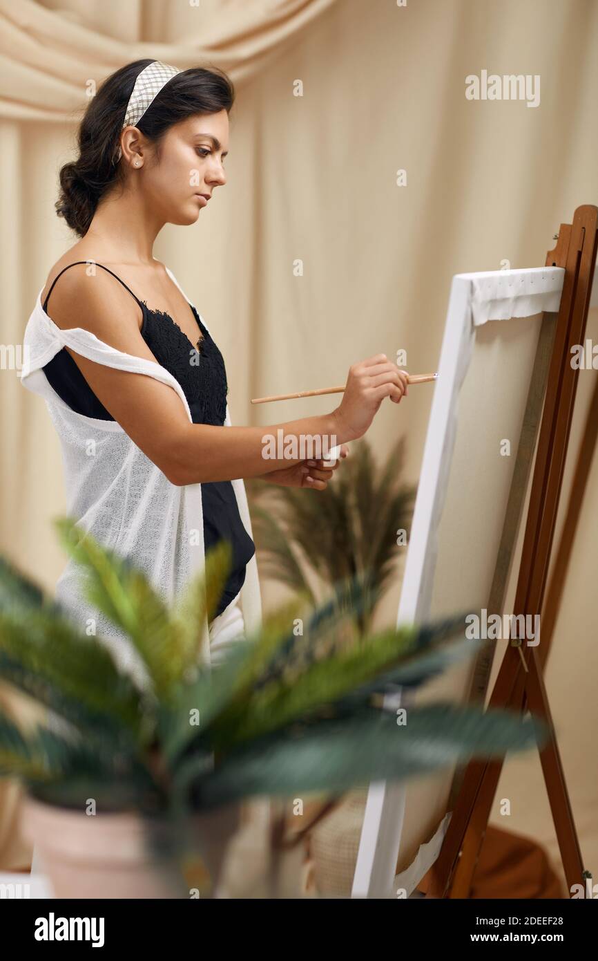 Young happy female artist in front of easel. Woman painting in art ...