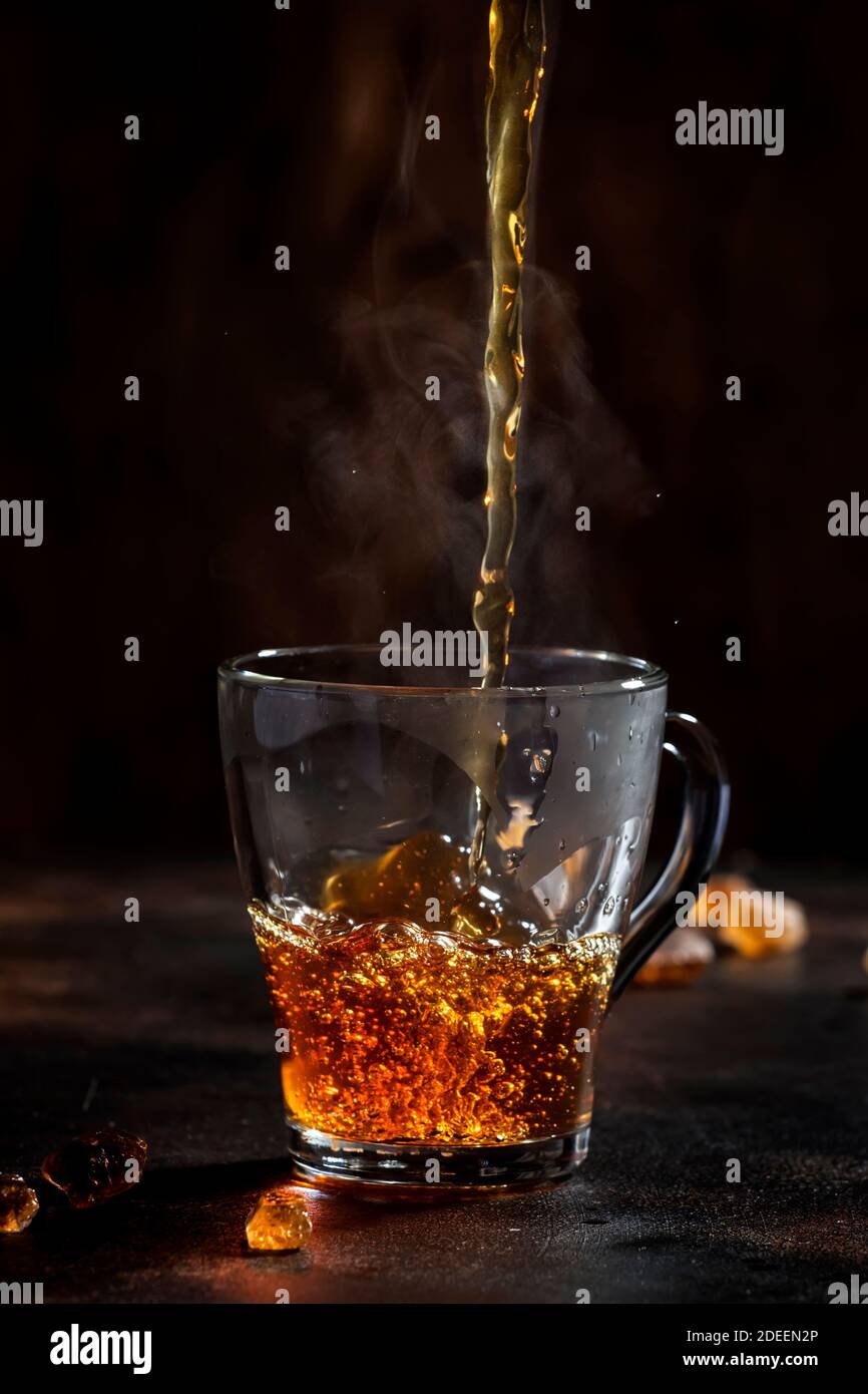 Black tea pouring into glass cup with natural steam on brown background ...