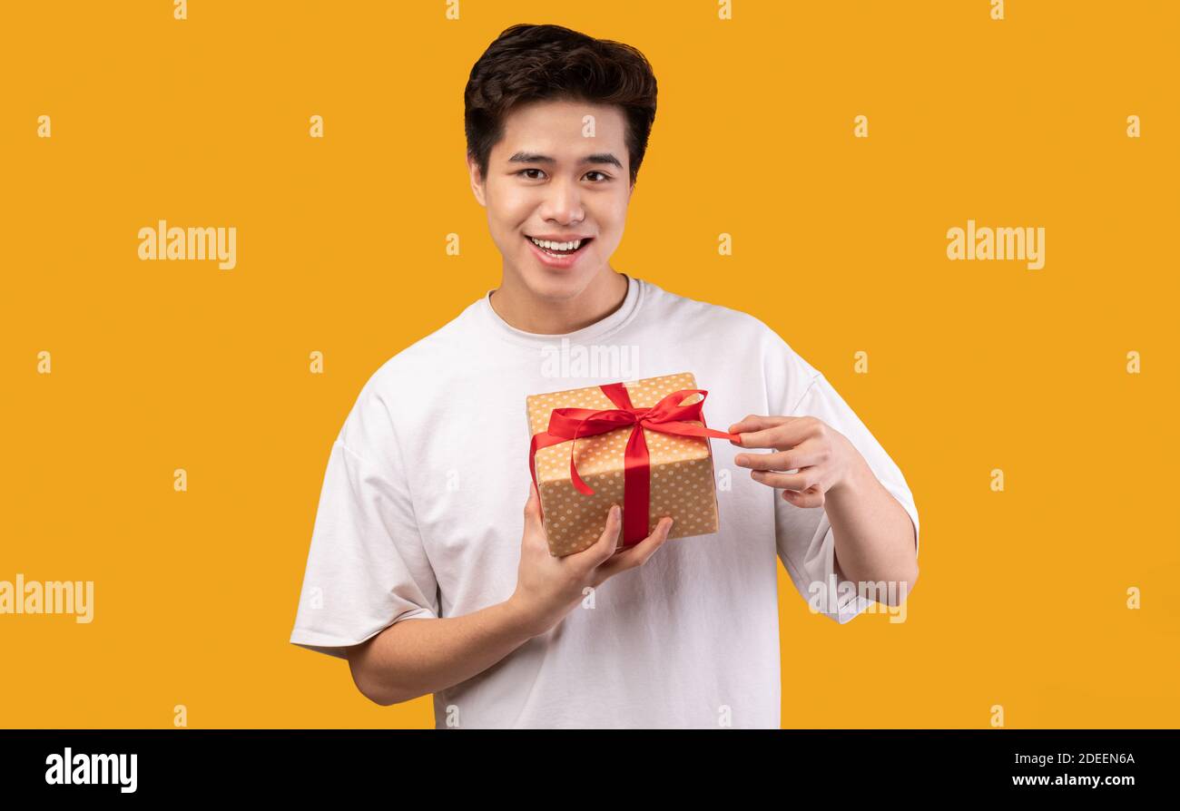 Happy asian guy holding present box pulling ribbon Stock Photo - Alamy