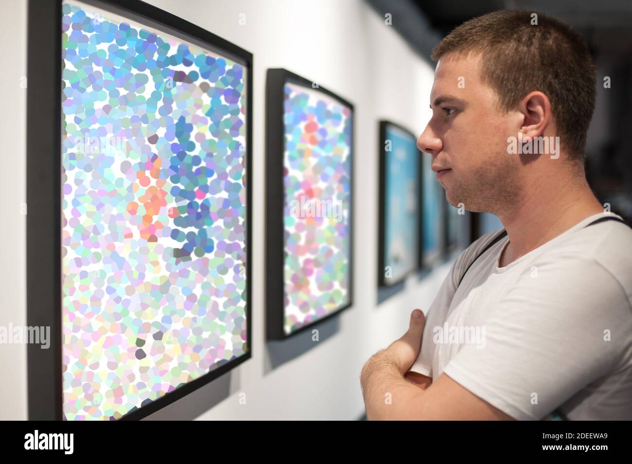 Young man in modern art exhibition gallery hall contemplating artwork ...