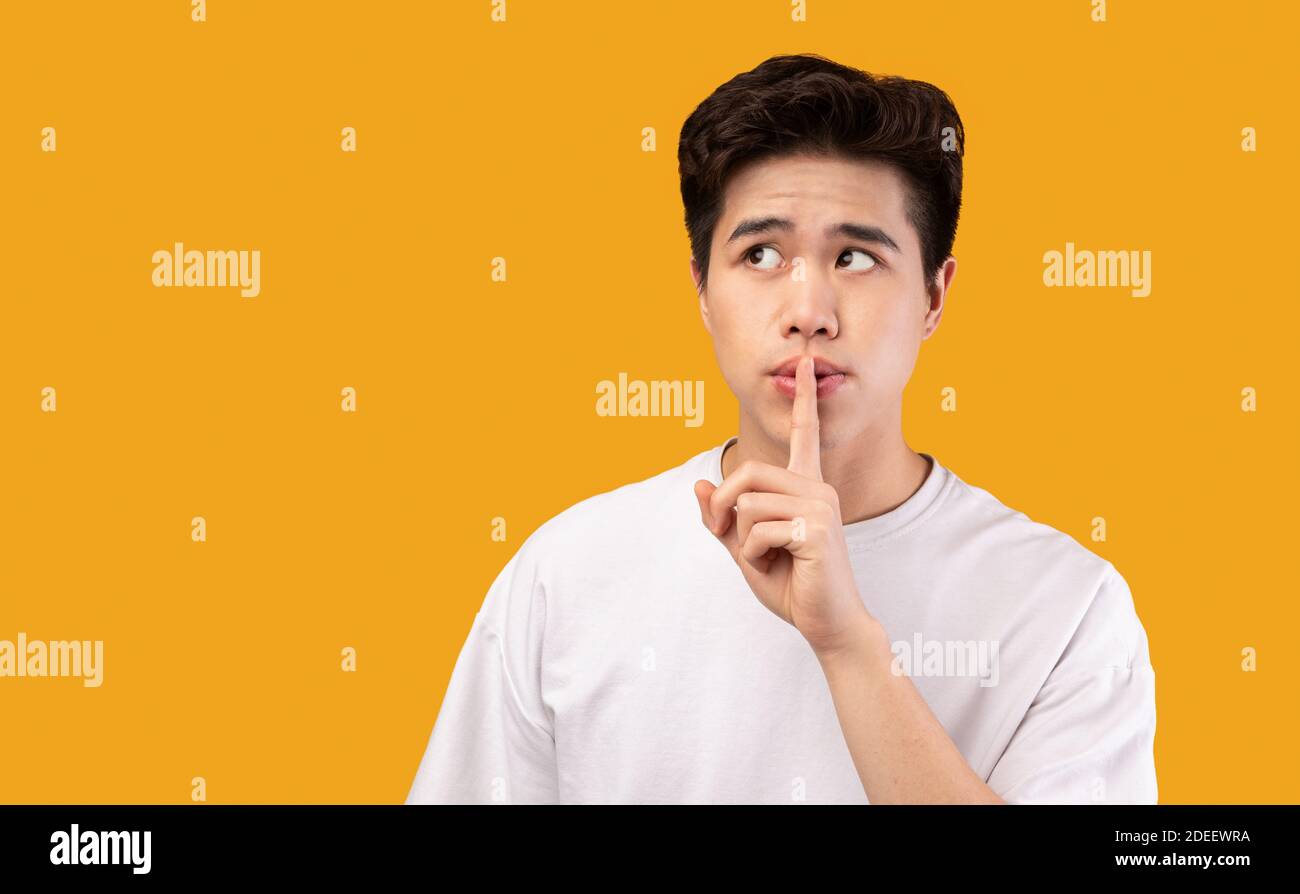 Asian man puting finger on his lips, making hush sign Stock Photo - Alamy