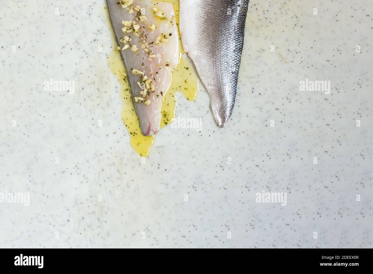 Two sea bass tails in green sauce with garlic, parsley, and oil on a ...