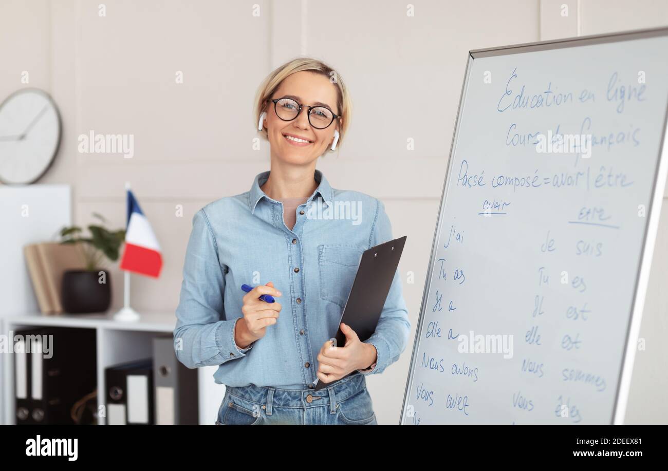 Friendly Young Female Tutor Standing Near Blackboard With French Grammar Rules Giving Web friendly-young-female-tutor-standing-near-blackboard-with-french-grammar-rules-giving-web