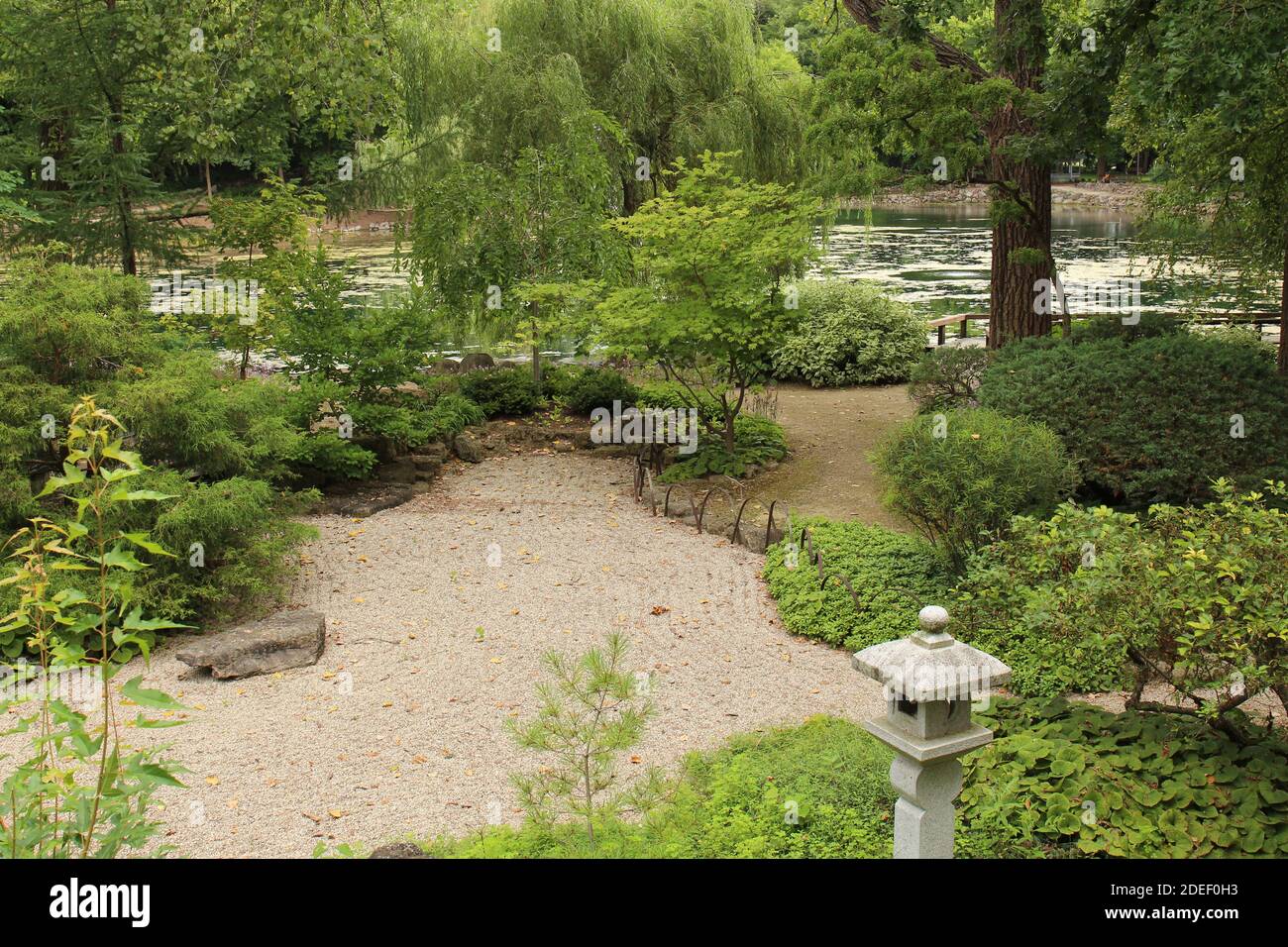 Raked stone garden surrounded by manicured shrubs and trees with a lake ...