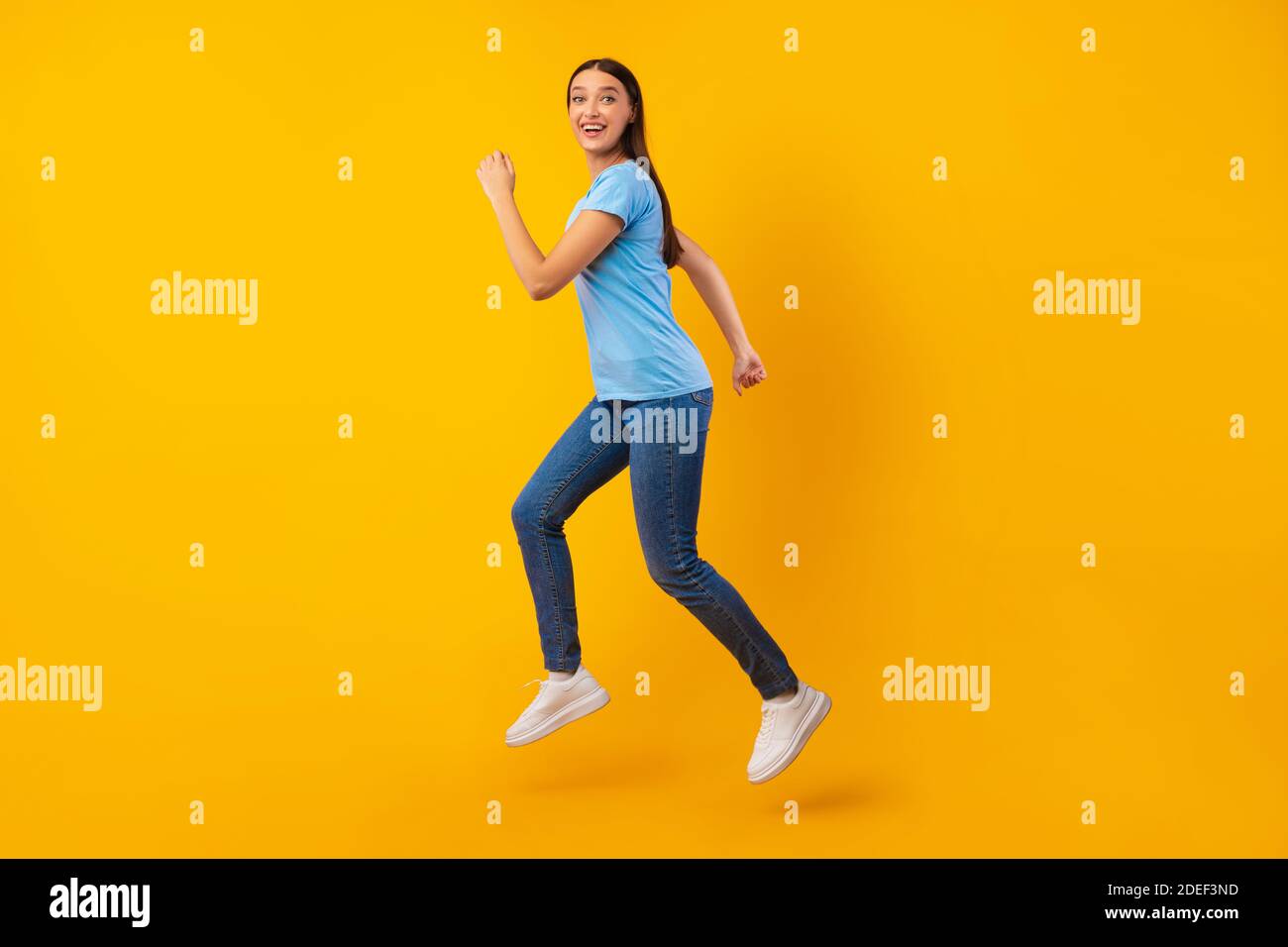 Happy lady jumping and running over yellow studio wall Stock Photo - Alamy