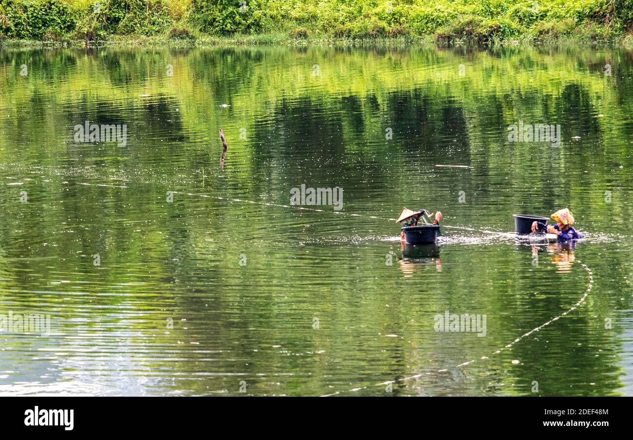 Men and women cockling and fishing in reservoir across from Likas Bay ...
