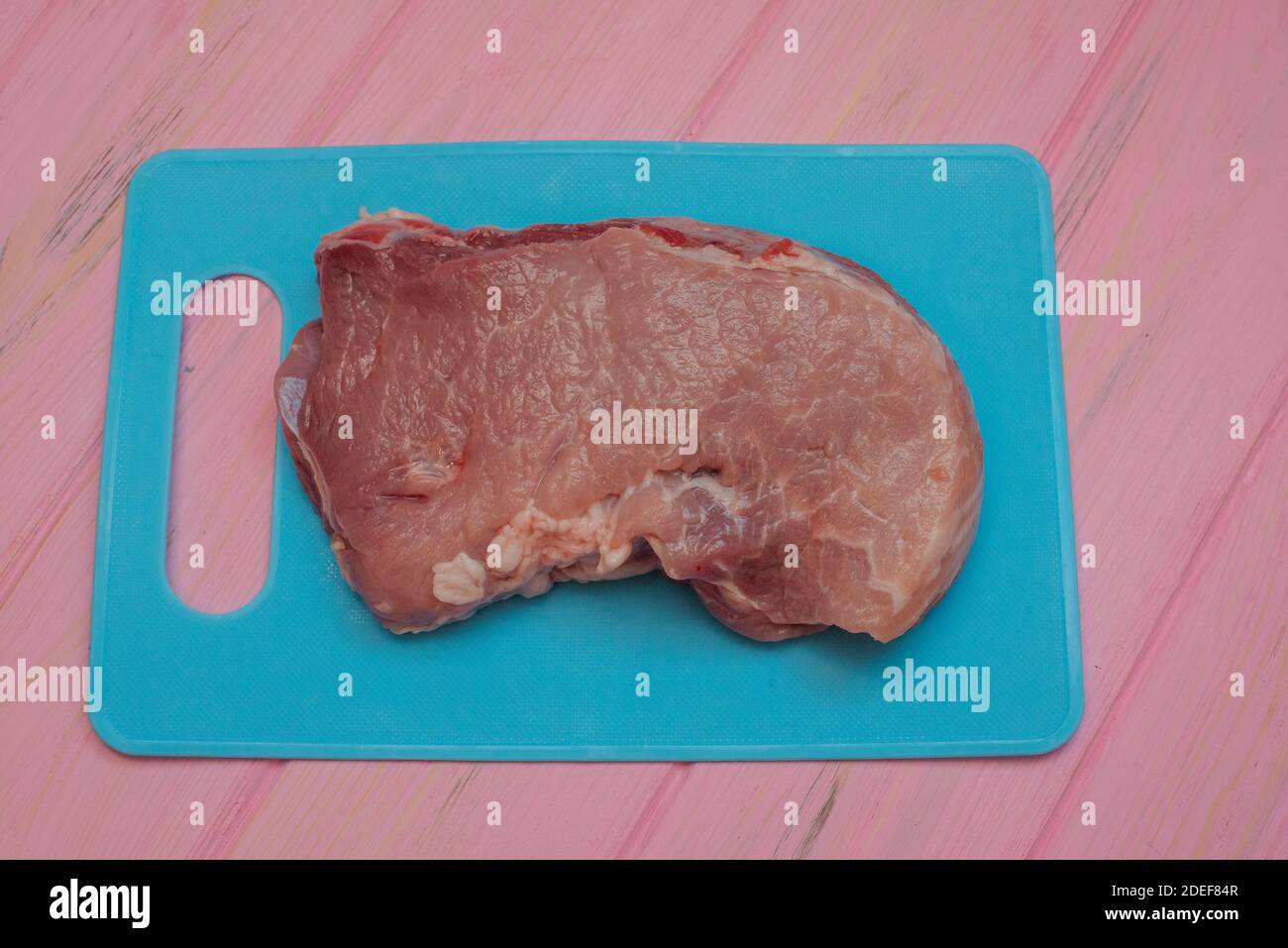 Pink raw pork steaks lie on a blue board. Appetizing meat. Pork on blue ...