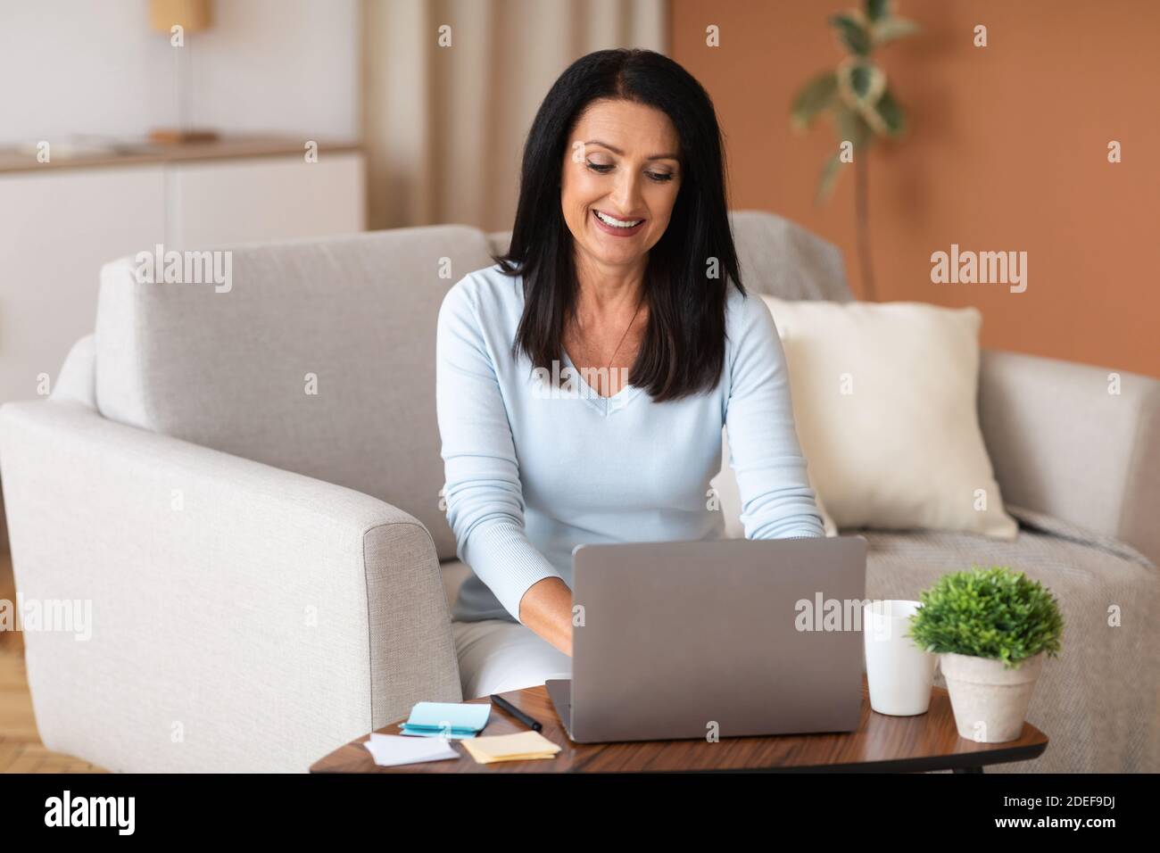 Mature woman sitting on couch and working on computer Stock Photo - Alamy