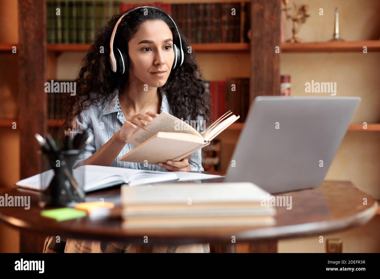 Woman sitting at desk, using computer and reading book Stock Photo - Alamy