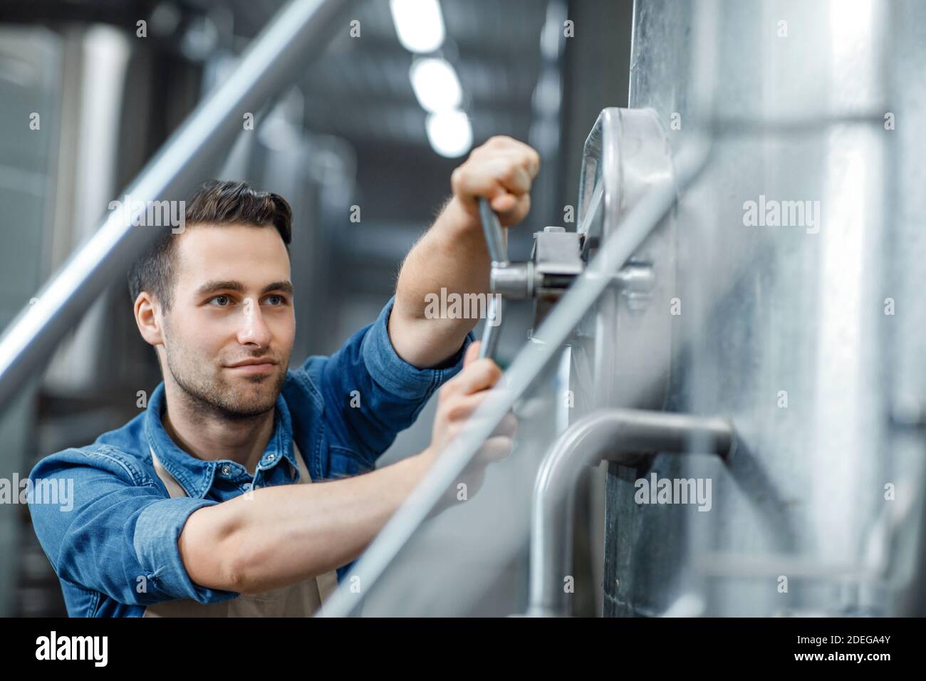 Millennial attractive male worker or owner in apron turns valve on big ...