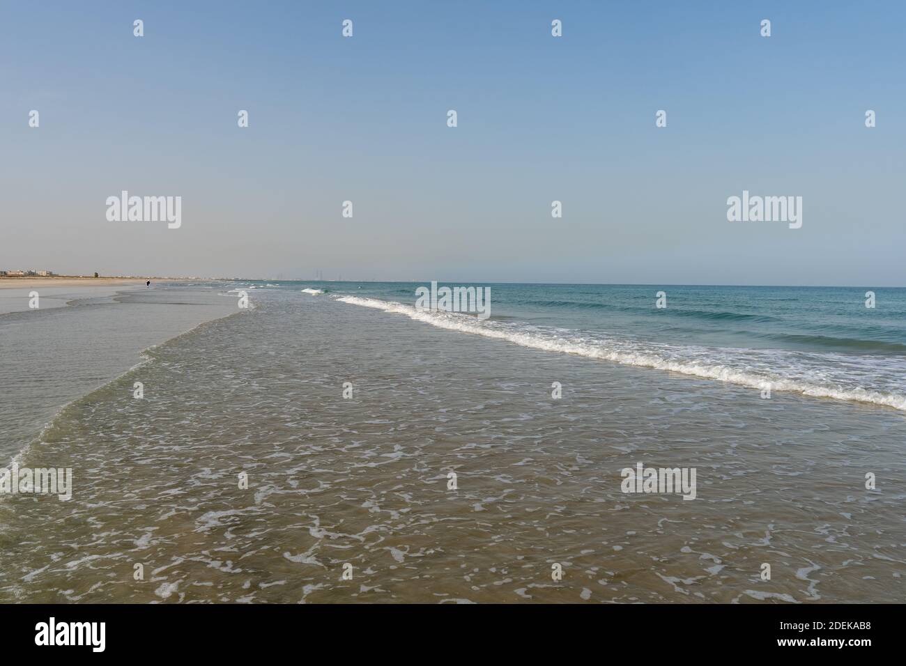 Gentle water tide waves comes in at a quiet beach with blue sky in the ...