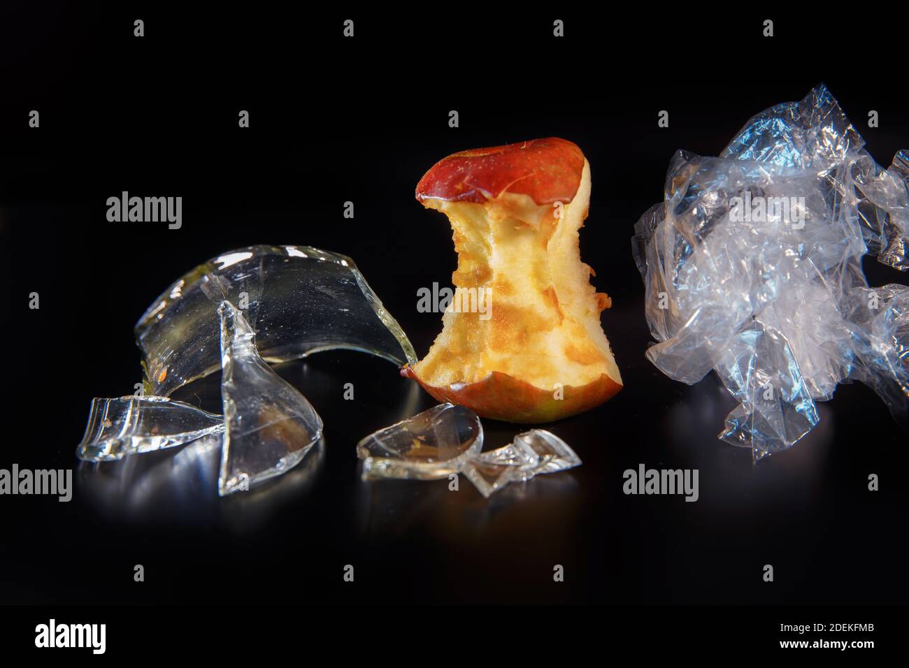 Apple core, polyethylene and glass shards on a black background with ...