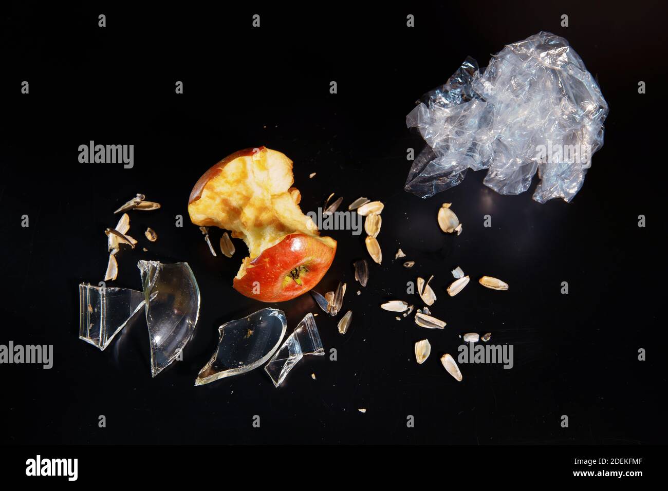 Apple core, polyethylene and glass shards on a black background with ...