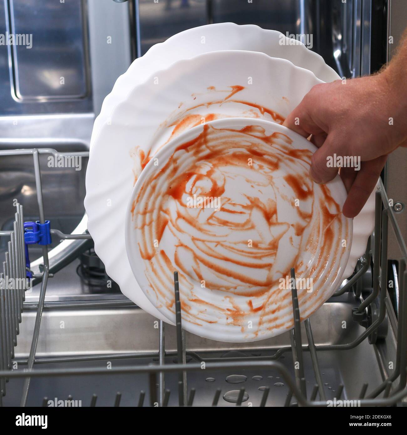 A man loads dirty dishes, plates, spoons, forks, cutlery into the ...