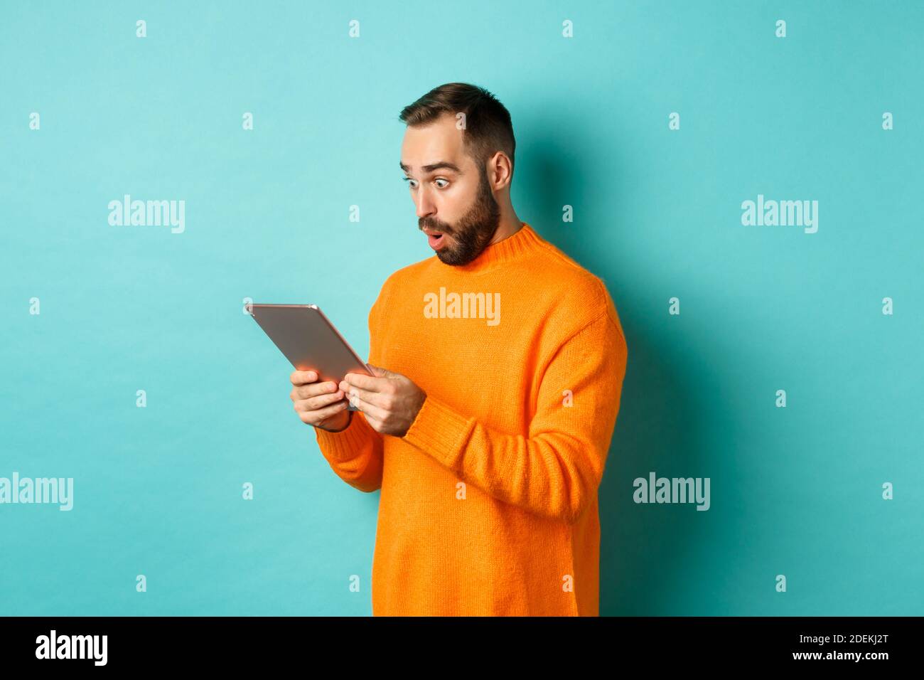 Image of male model in orange sweater staring at digital tablet screen ...