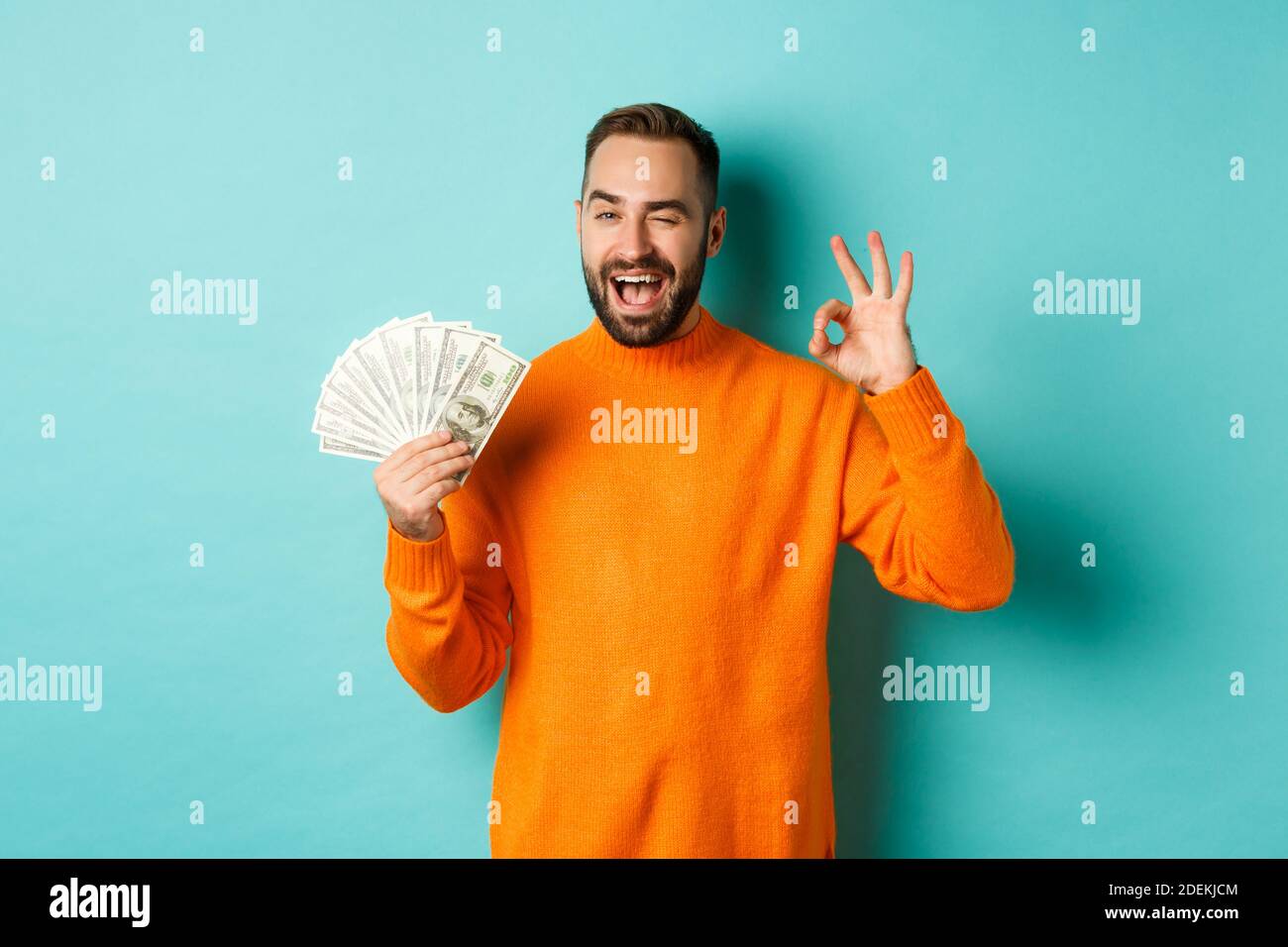 Shopping. Excited guy holding money, showing ok sign and winking ...