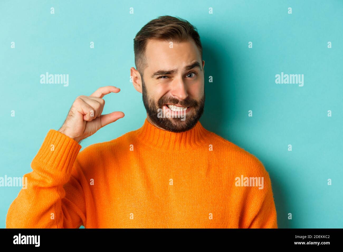 Close-up of awkward man showing small or little with fingers, standing ...