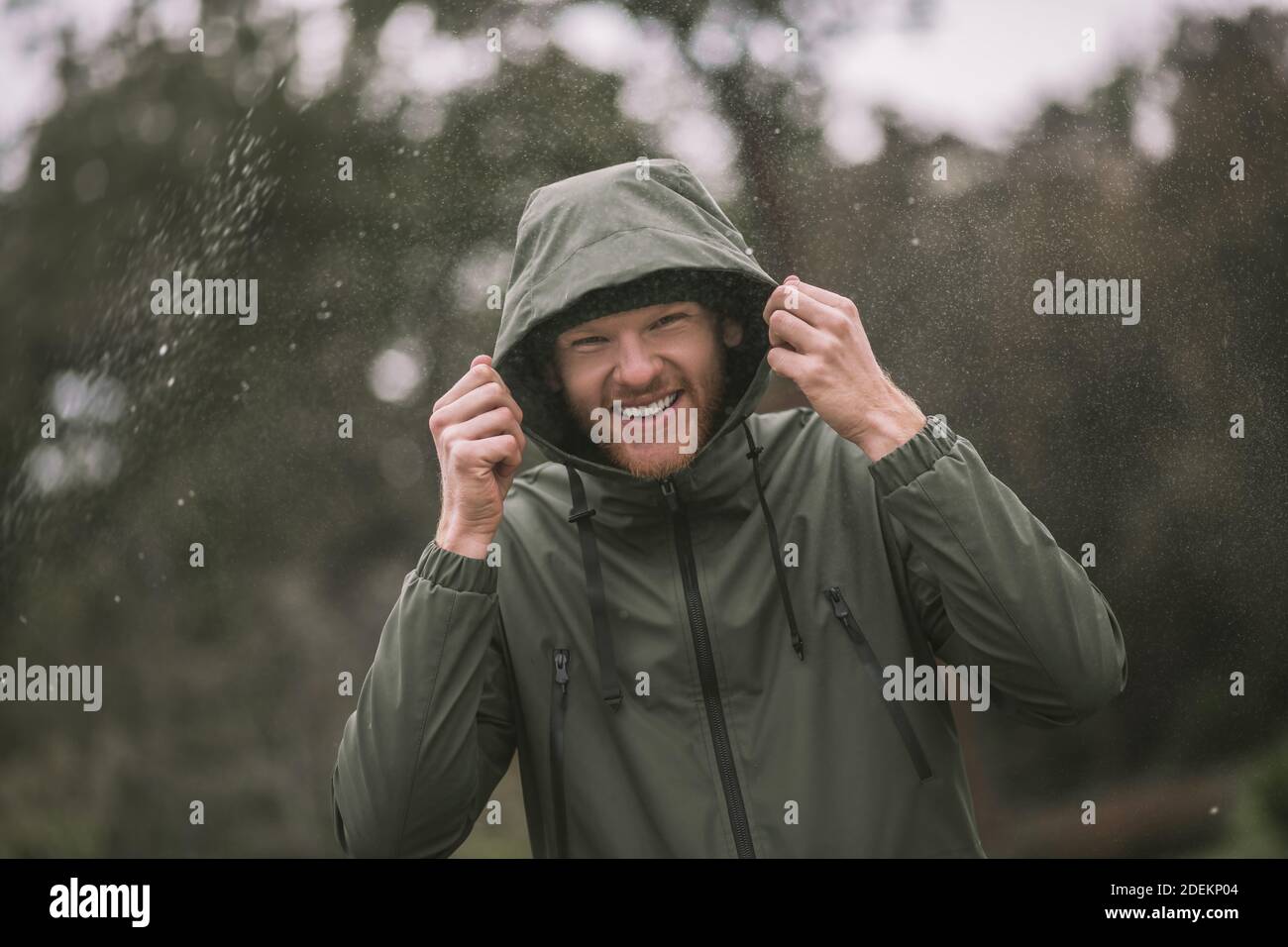 Young man in a green coat walking in the rain and smiling Stock Photo ...