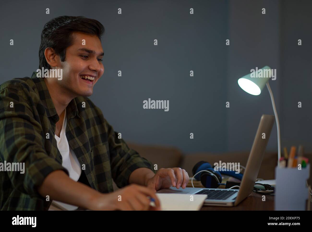 College student talking on a video call while writing his assignment ...