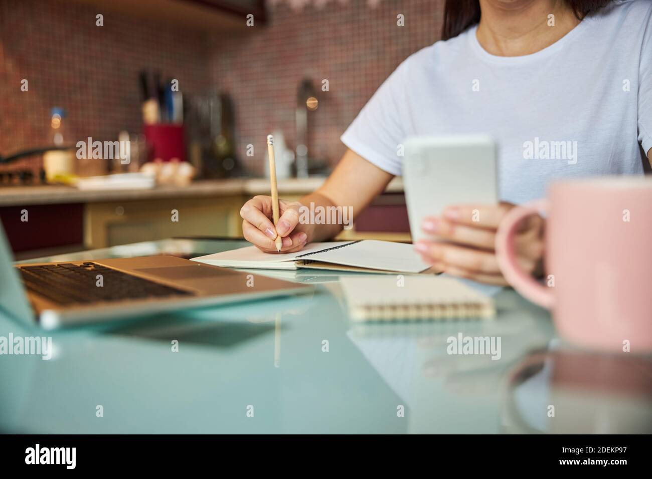 Employee taking notes from smartphone to her notebook Stock Photo - Alamy
