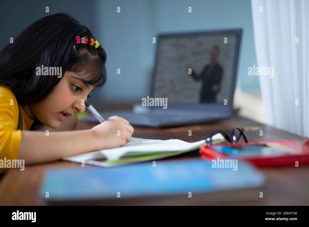 Young girl doing her work while attending virtual class Stock Photo - Alamy