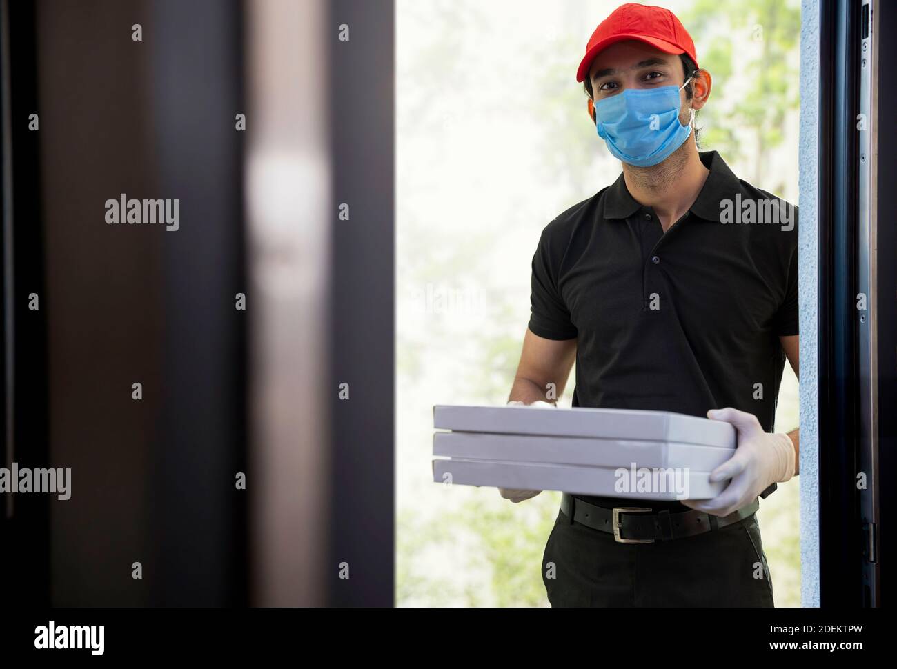 Portrait of a pizza delivery boy standing at the door wearing facemask ...