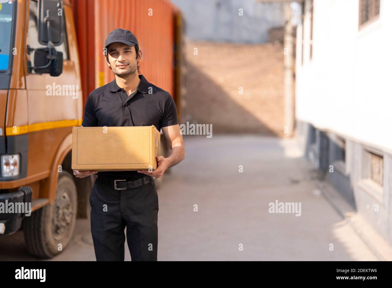 Courier boy standing with a parcel in his hand and smiling Stock Photo ...