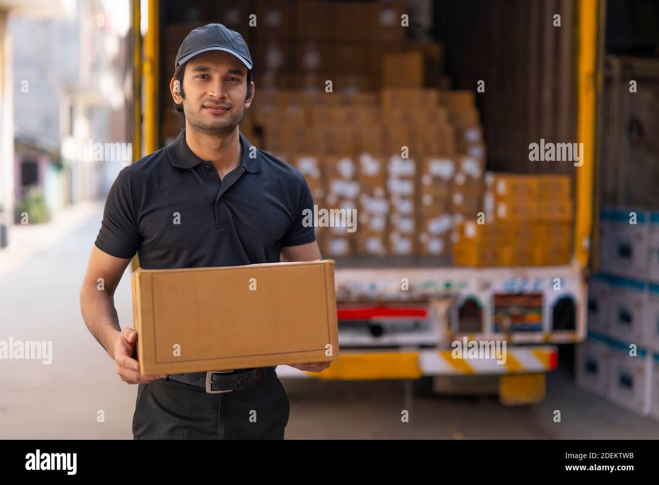 Courier boy standing with a parcel in his hand and smiling Stock Photo ...