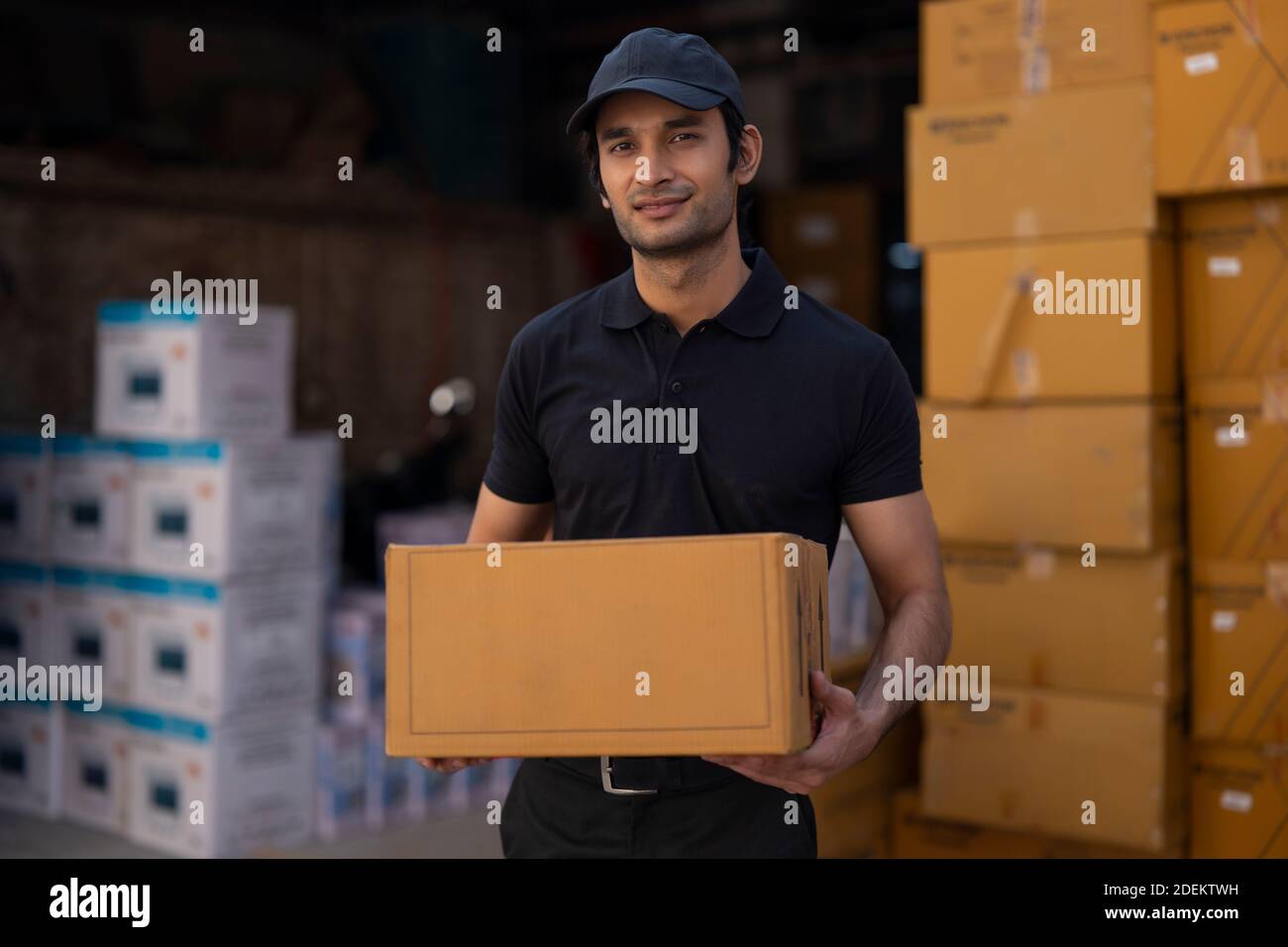 Courier boy standing with a parcel in his hand and smiling Stock Photo ...