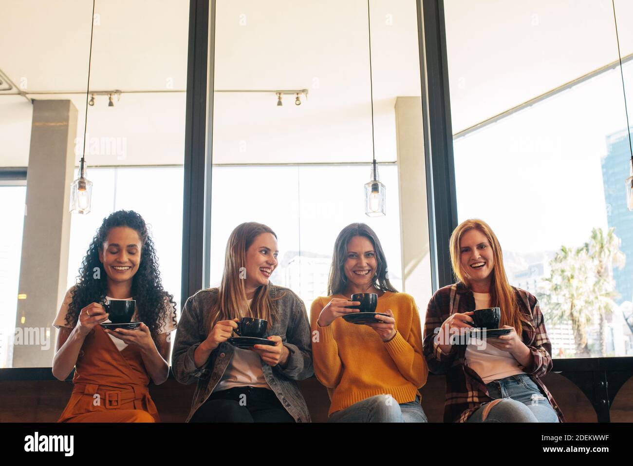 Four female friends sitting in a row and smiling in a coffee shop ...