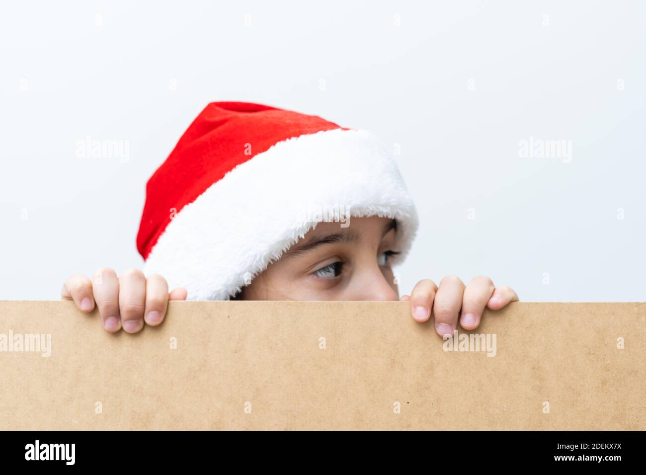 Happy little girl child in Santa hat peeking from behind blank sign ...