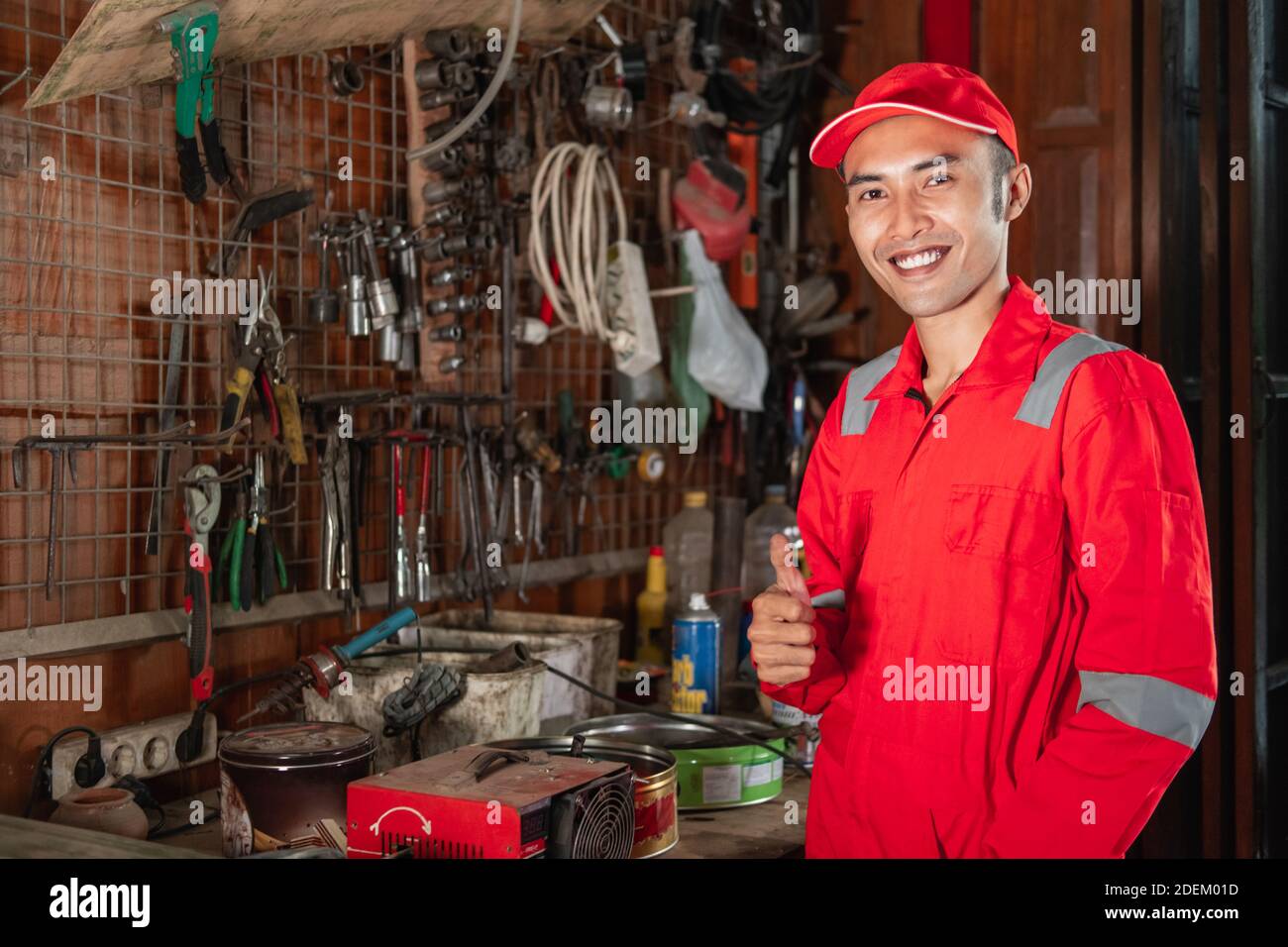 smiling mechanic in wearpack uniform with thumbs up standing in garage ...