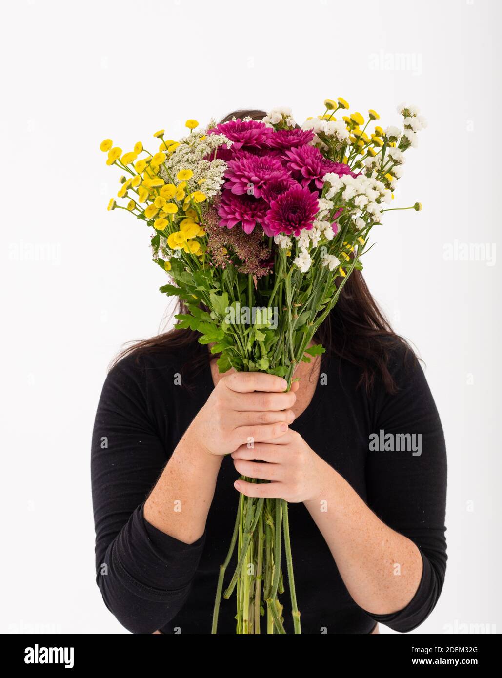 Caucasian woman covering her face with bouquet of flowers on white ...