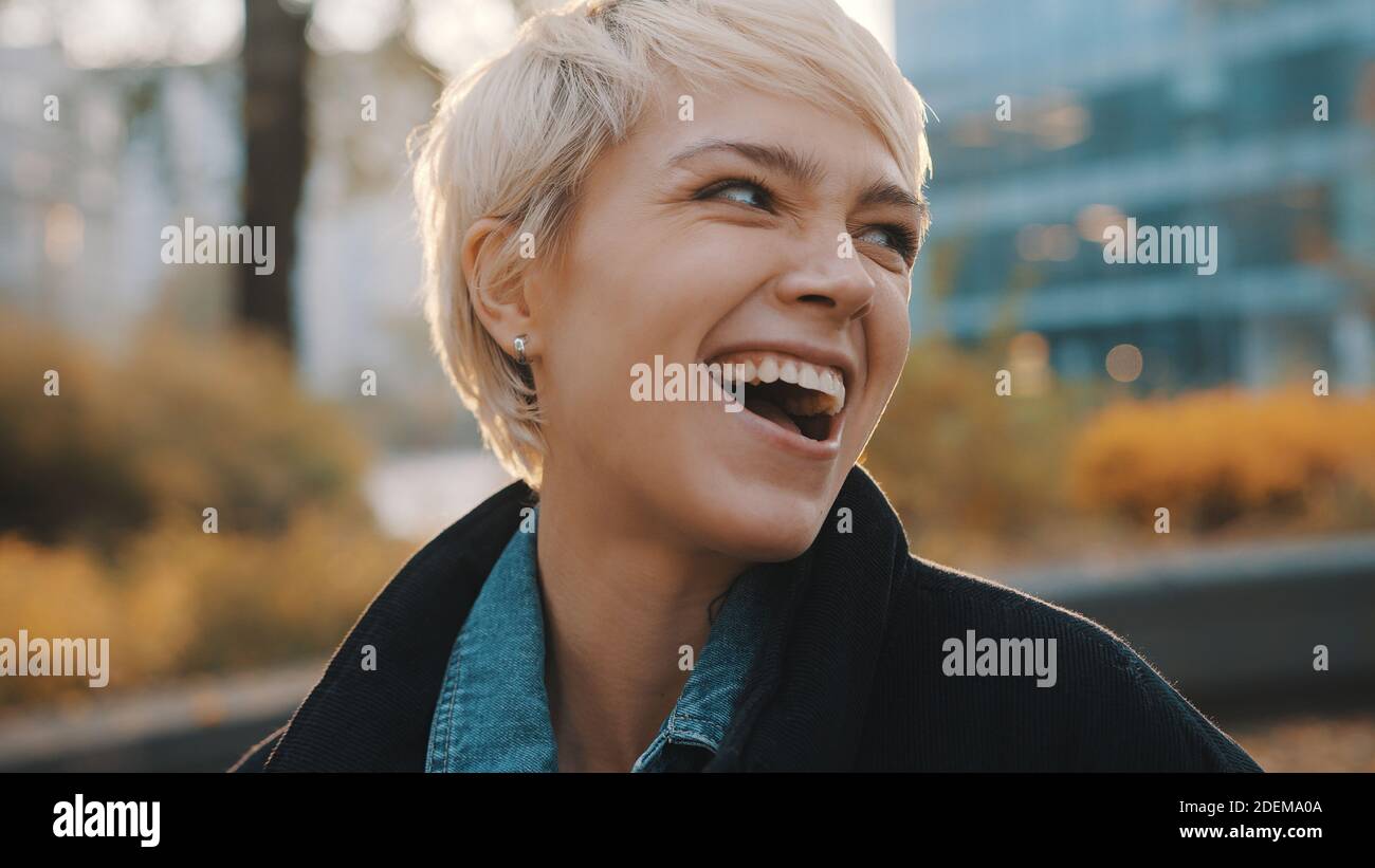Beautiful excited young caucasian blond woman laughing in the city park ...
