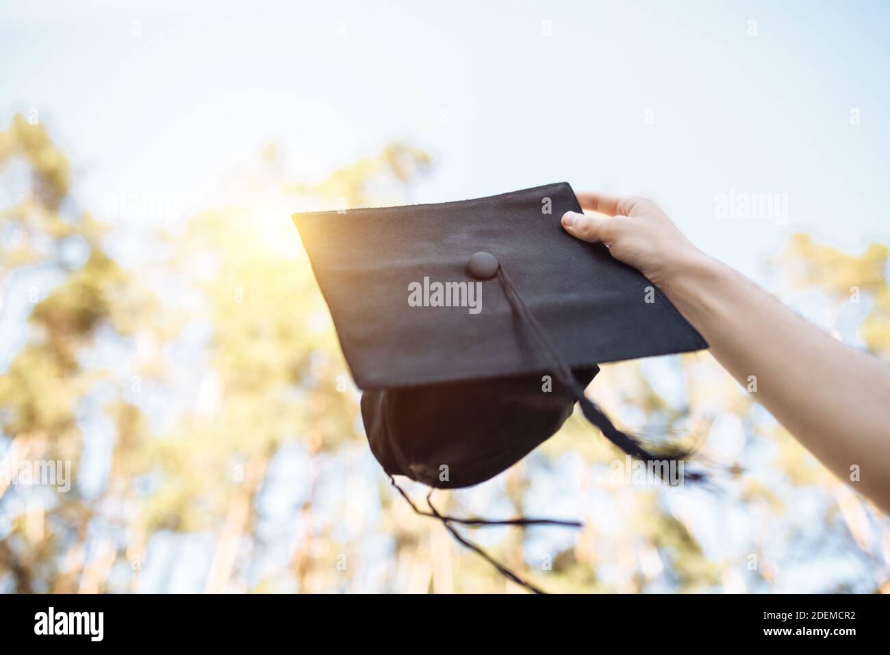 Successful graduate, in academic dresses, raised up graduation cap ...