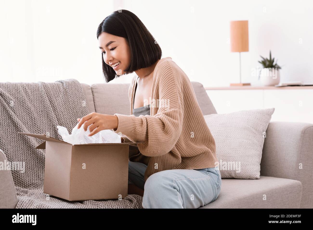 Happy asian woman unpacking parcel sitting on couch Stock Photo - Alamy