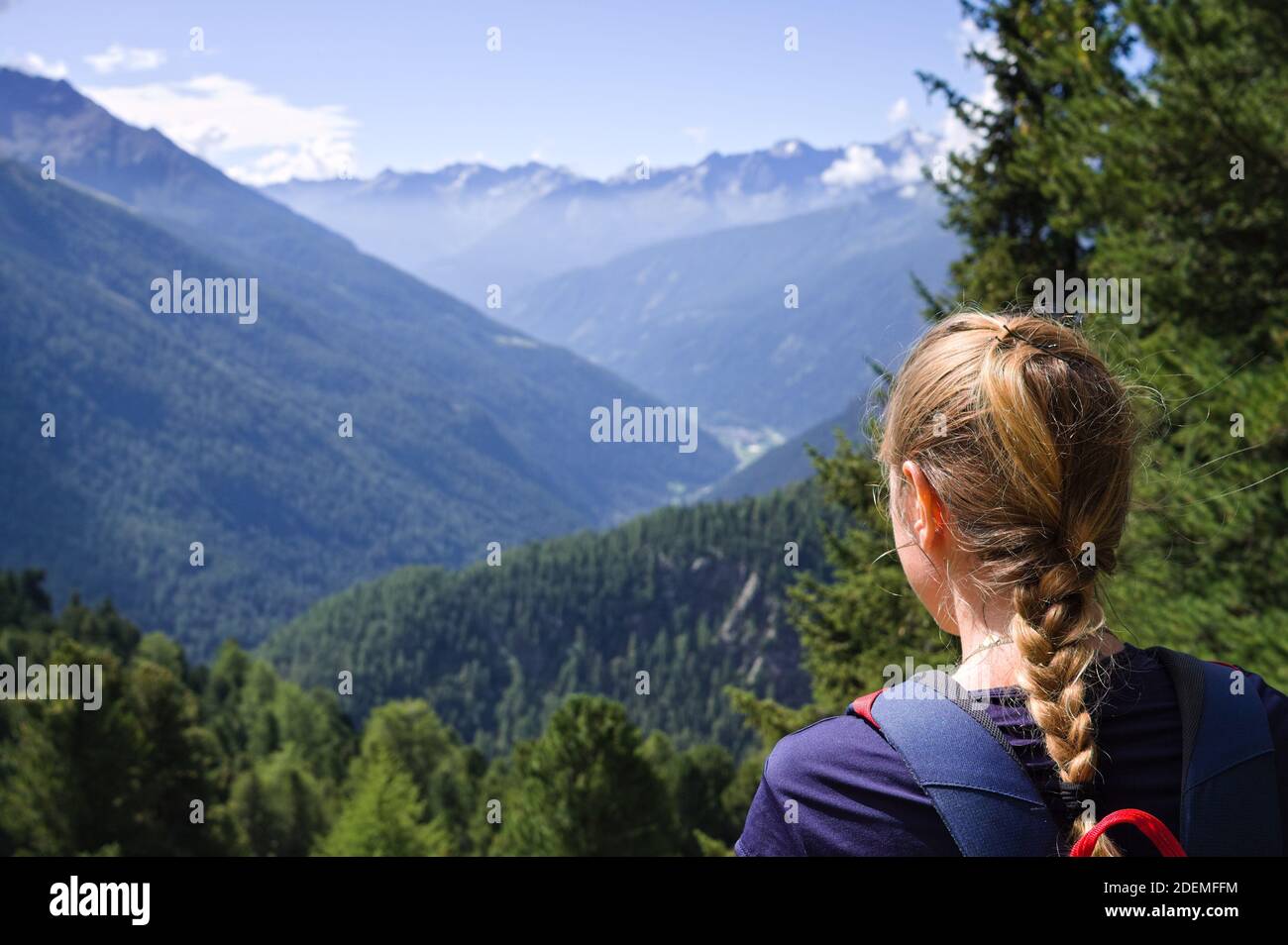 A blonde young girl is watching the panorama in the italian Alps ...
