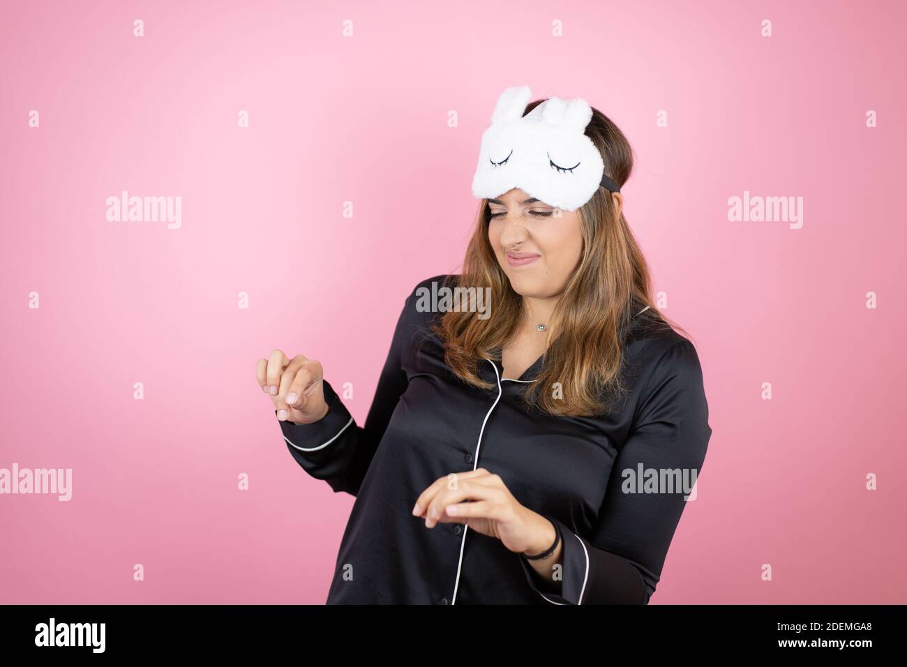 Young caucasian woman wearing sleep mask and pajamas over isolated pink ...