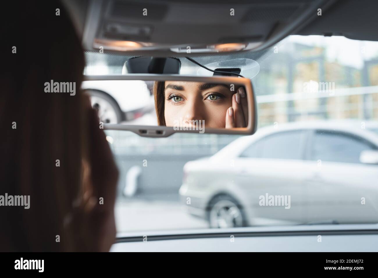 woman in car touching face while looking in rearview mirror on blurred ...