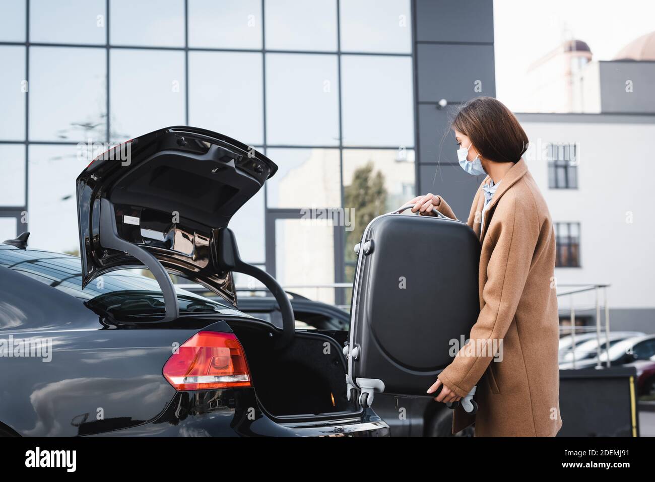 young woman in medical mask loading suitcase in car trunk Stock Photo ...
