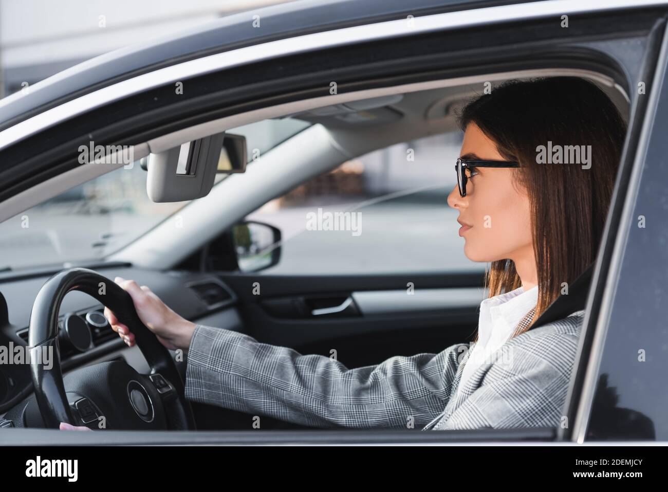 side view of businesswoman in eyeglasses looking ahead while driving ...