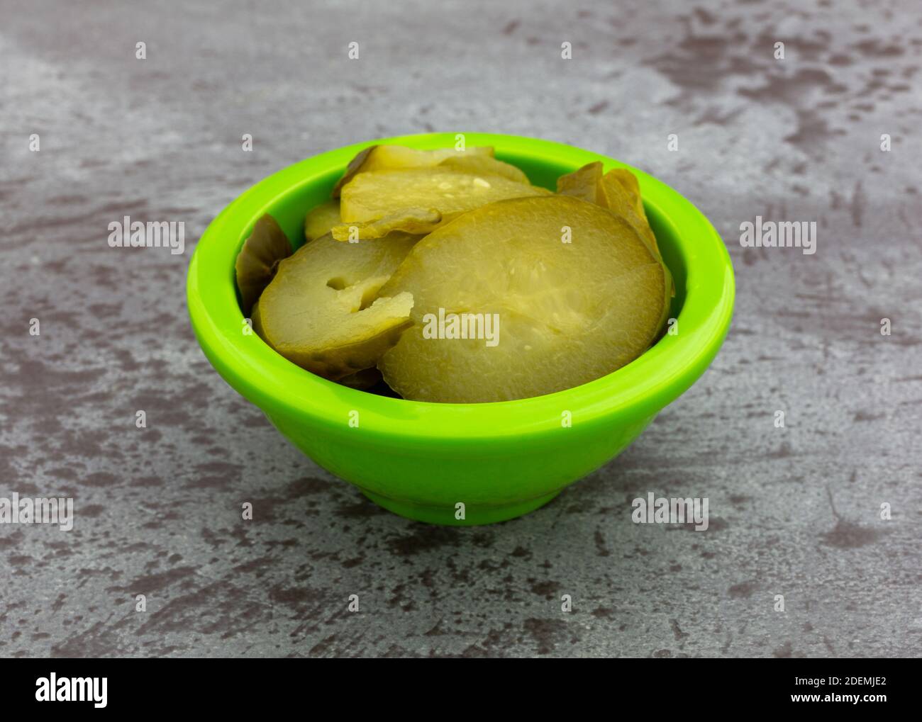 Side view of a small green bowl filled with cucumber salad atop a gray ...