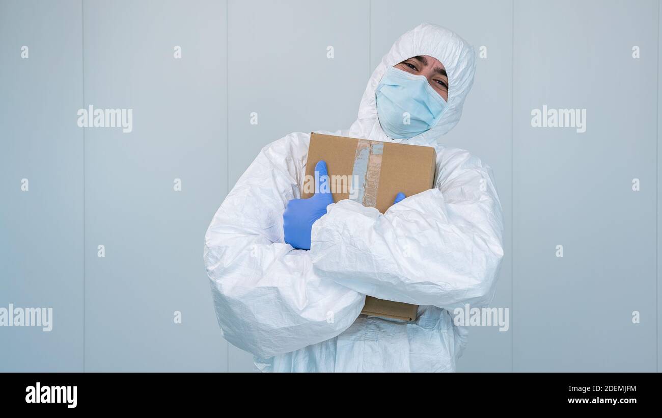 A happy health worker on protective suit hug a box of medical supplies ...