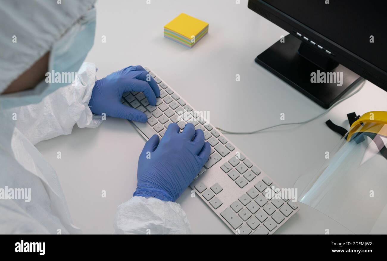 A nurse in a protective suit PPE typing on a computer inside a hospital ...