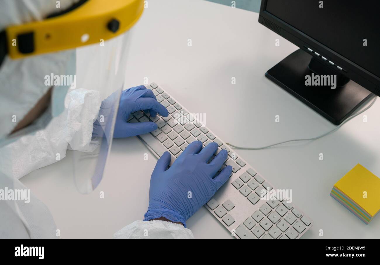 A nurse in a protective suit PPE and face mask typing on a computer ...
