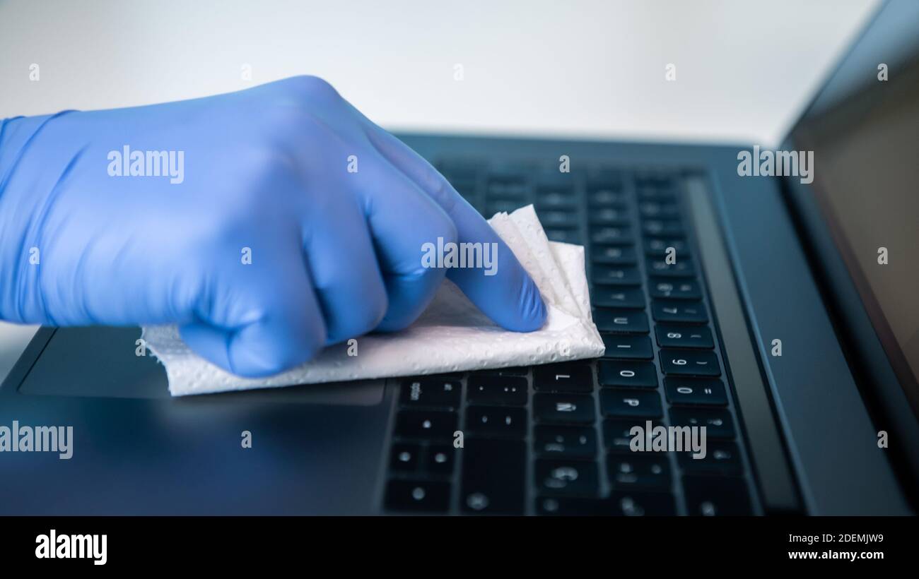 Person cleaning and disinfecting the keyboard of a laptop with gloves ...