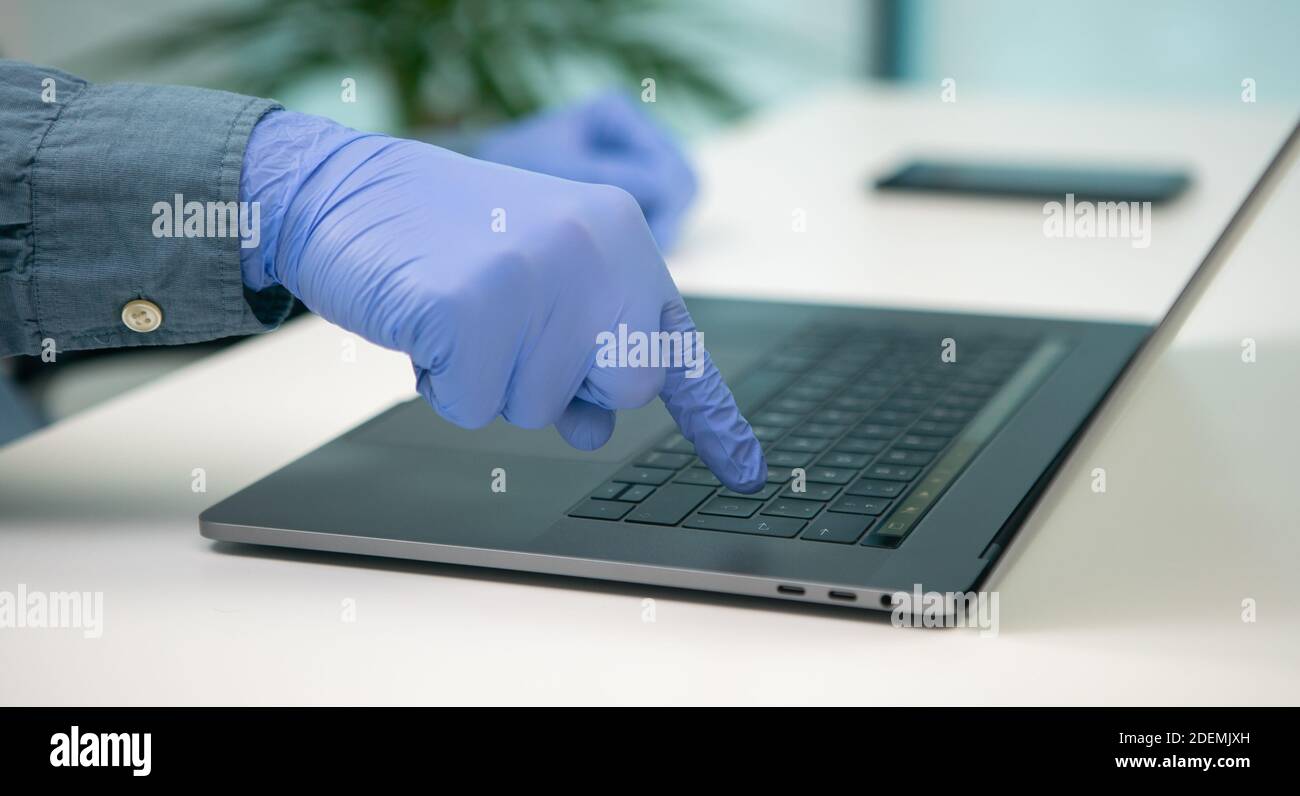 Person with gloves on his hands pressing the enter key on his laptop ...