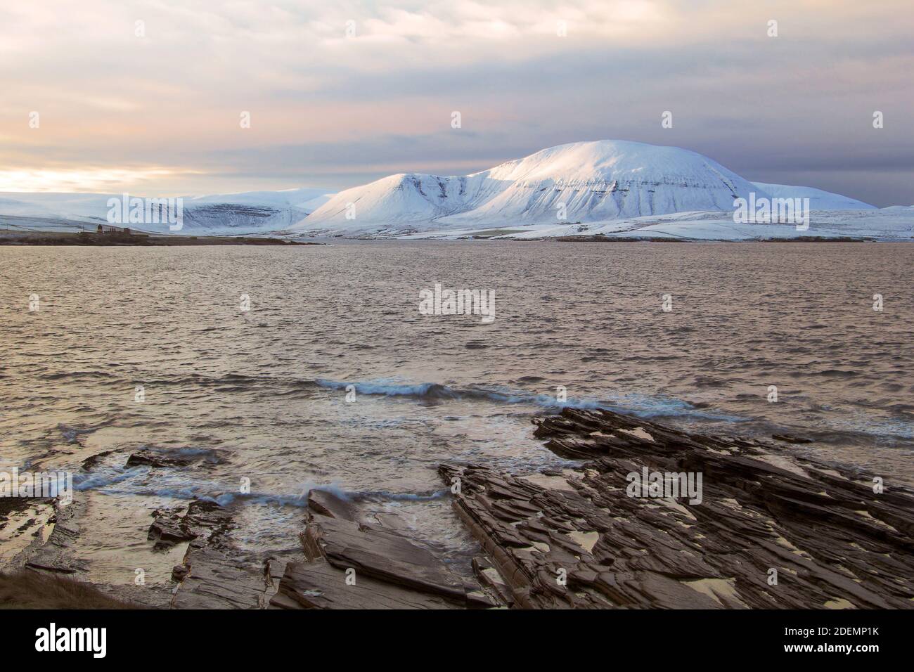 Orkney coast in winter scene with big hill under snow and calm waters ...